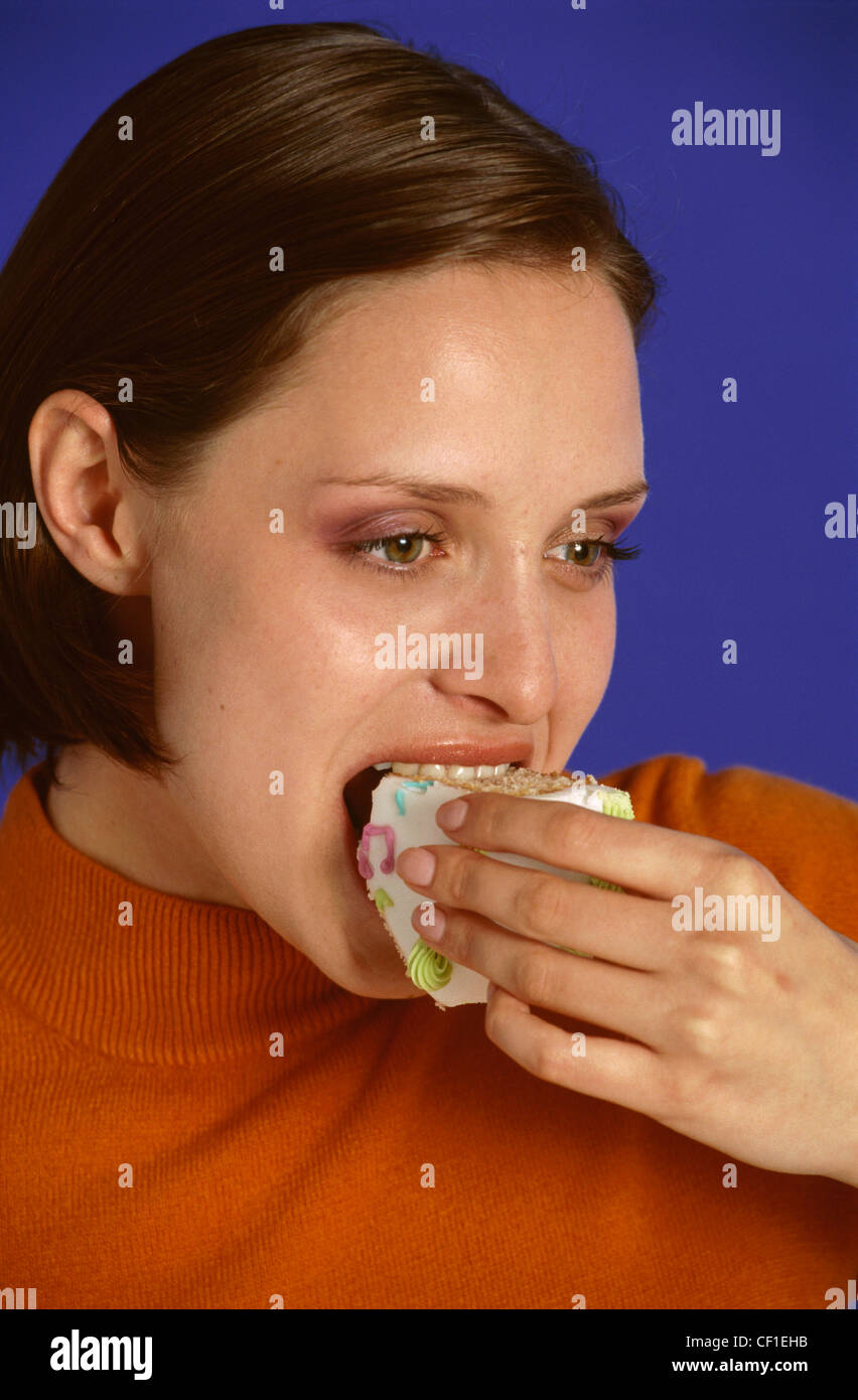 Female with short brunette hair, wearing an orange top, biting a slice ...