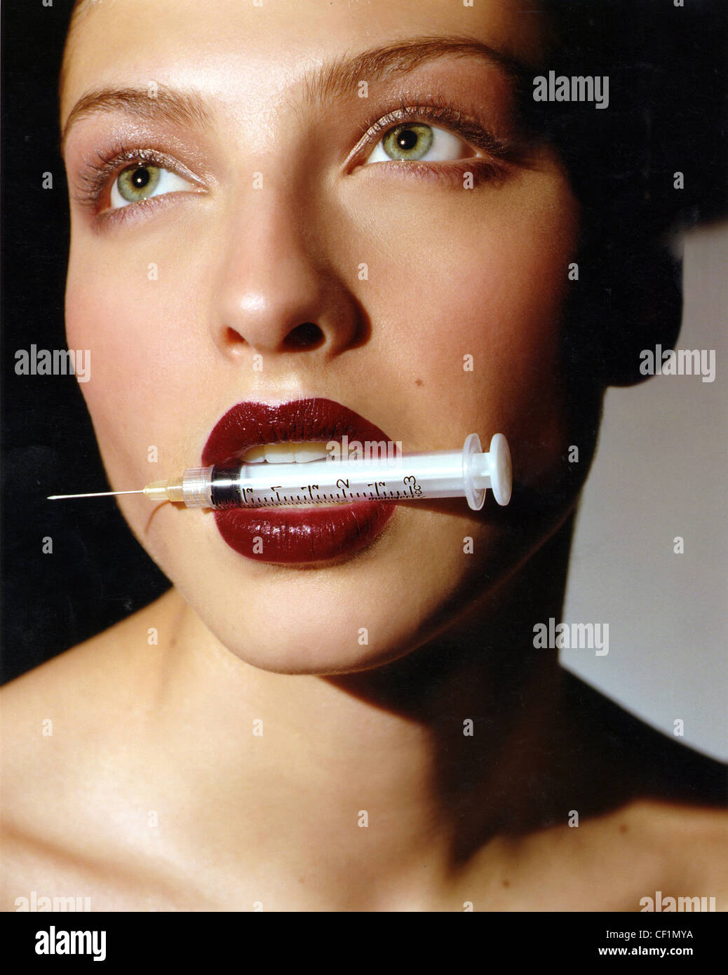 Female wearing deep berry red lipstick, holding a syringe between her ...