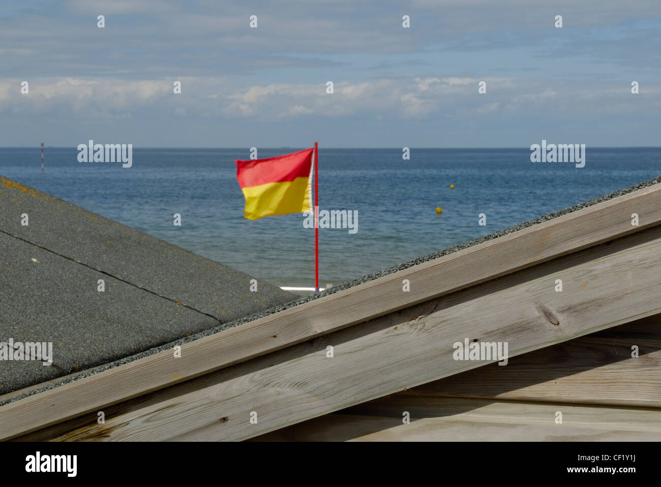 A bathing flag seen between the roofs of two beach huts. The bathing ...