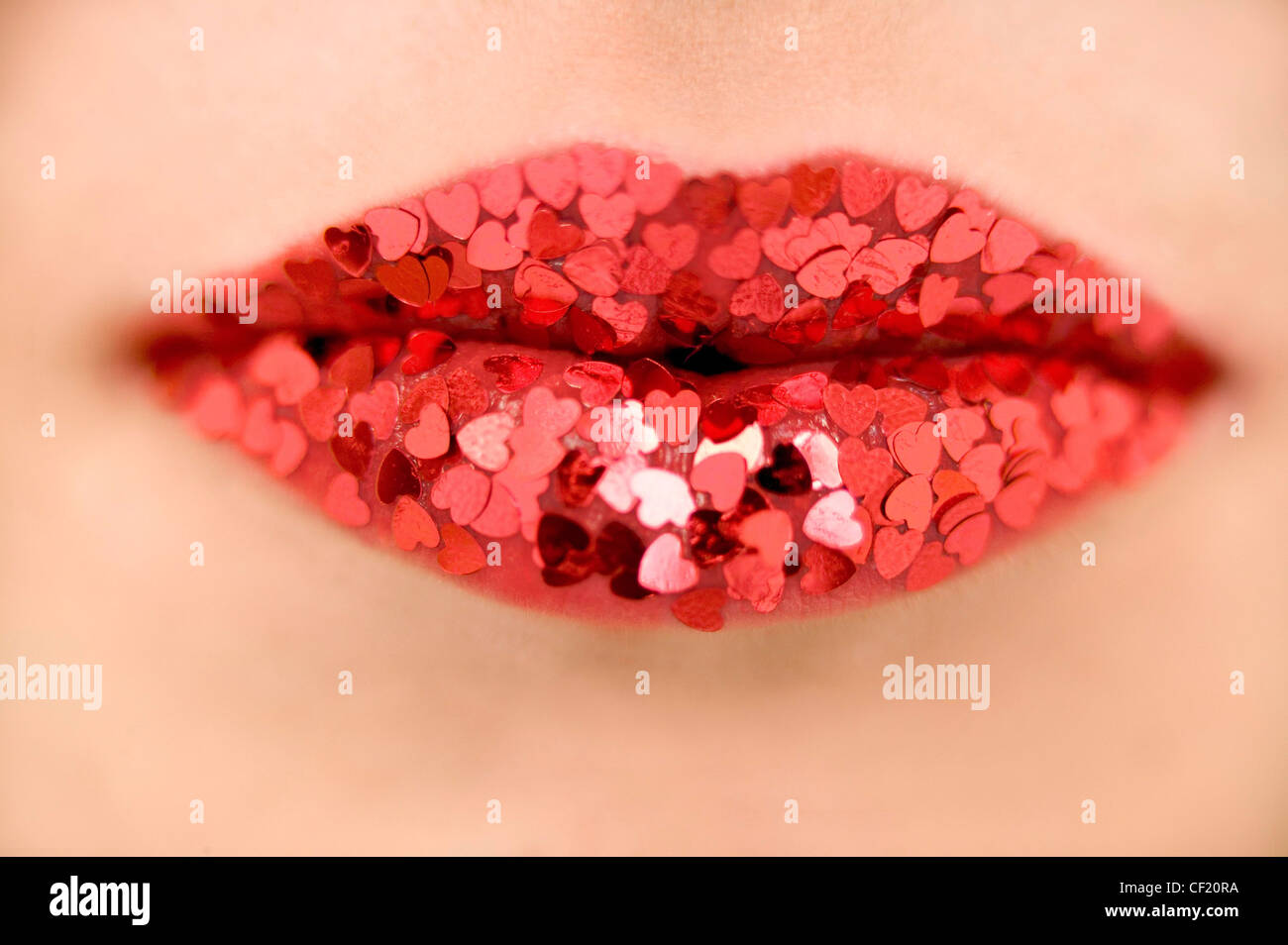 Close up lips of female with red lipstick and small metallic red hearts ...