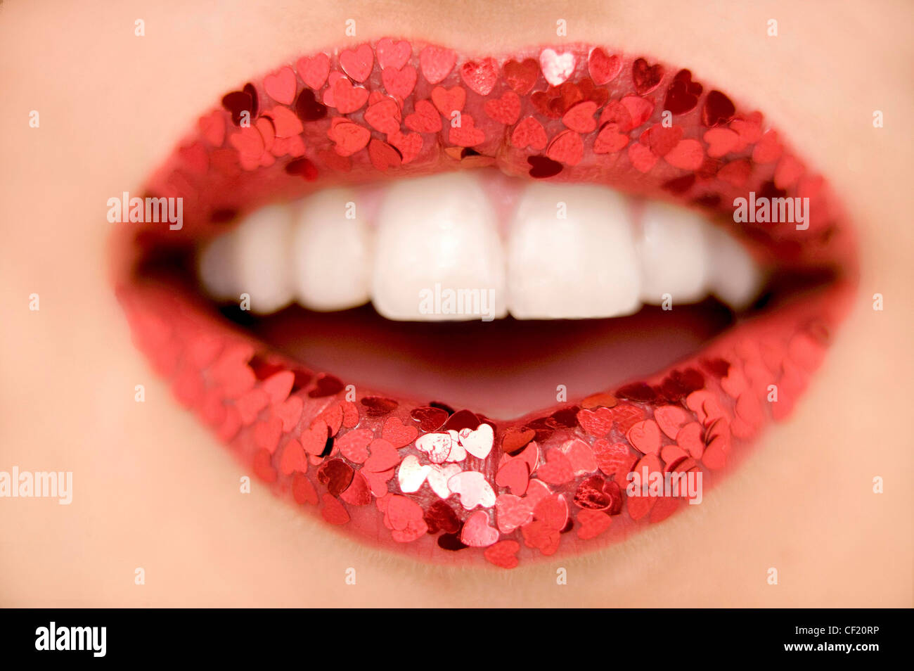 Close up lips of female with red lipstick and small metallic red hearts ...