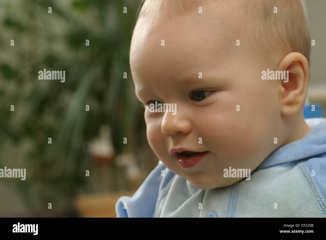 Semi profile of male baby wearing blue top looking down half smiling ...