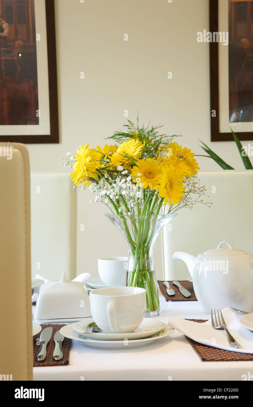 A table laid ready for breakfast, with white crockery, miniature jams ...