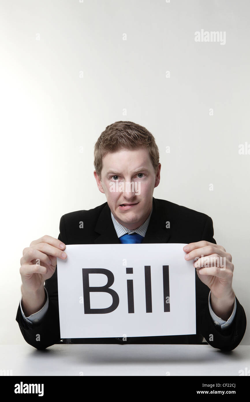 man in a suit sat at a desk look at a piece of paper with the word bill ...