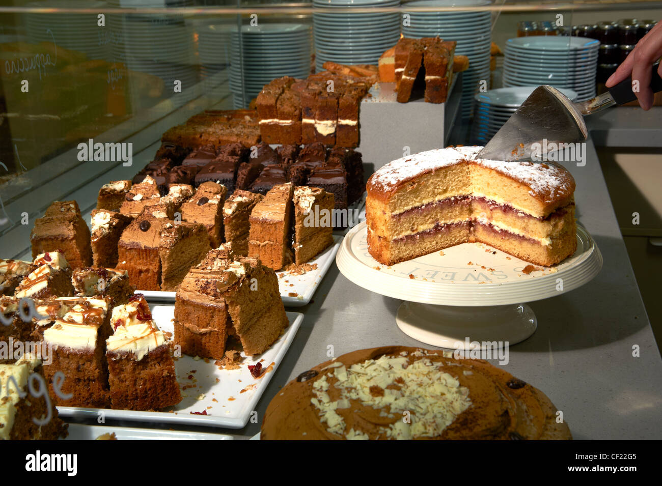 A display of cakes to sell, one sponge being cut ready for serving ...