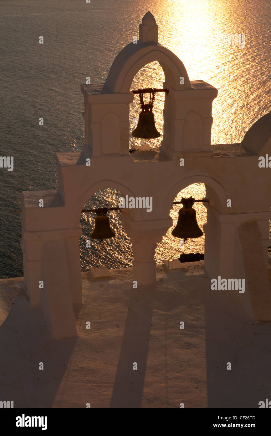 A view of a traditional bell tower at sunset with the caldera and sea ...