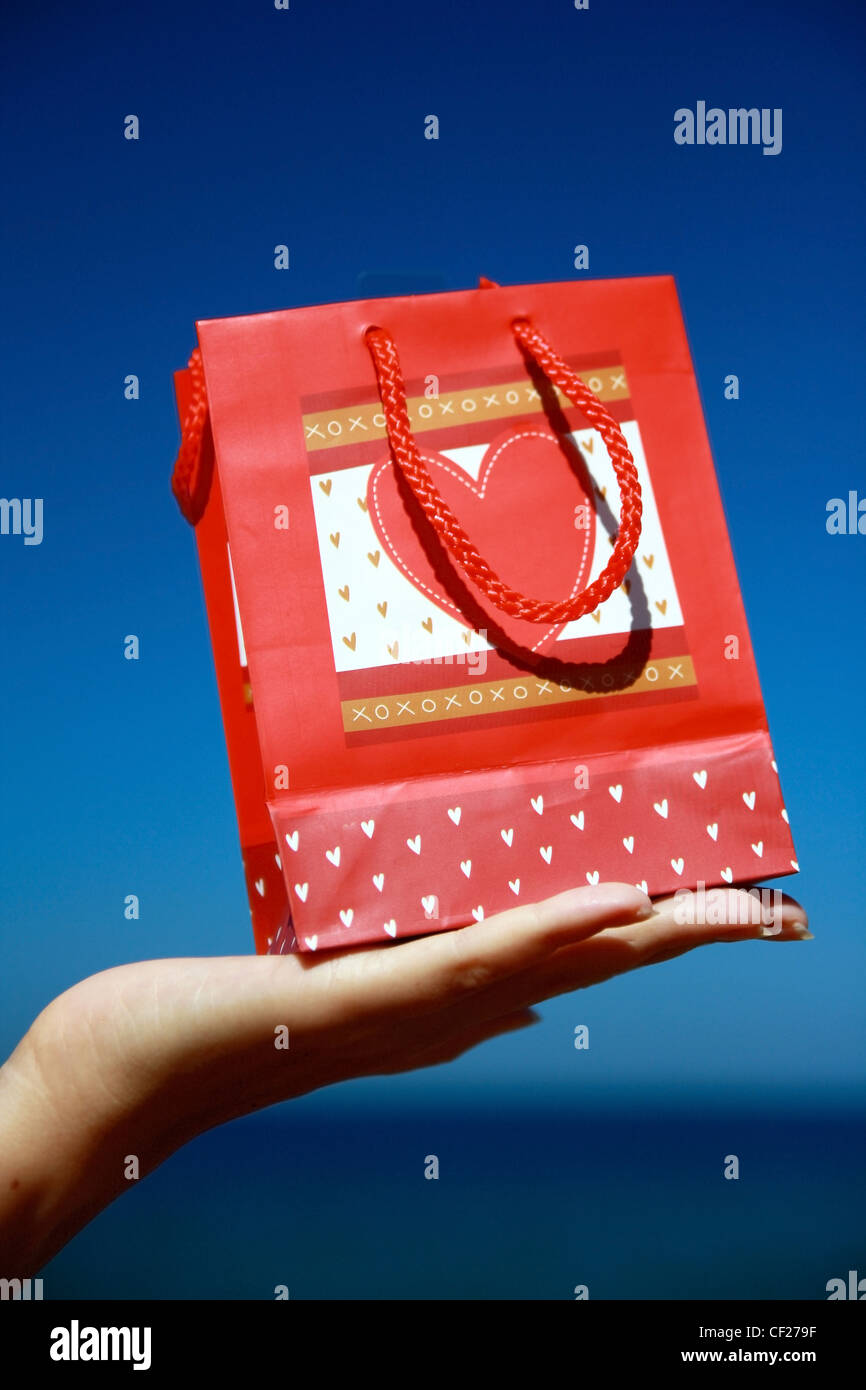 Present with heart in hand on blue sky background Stock Photo - Alamy