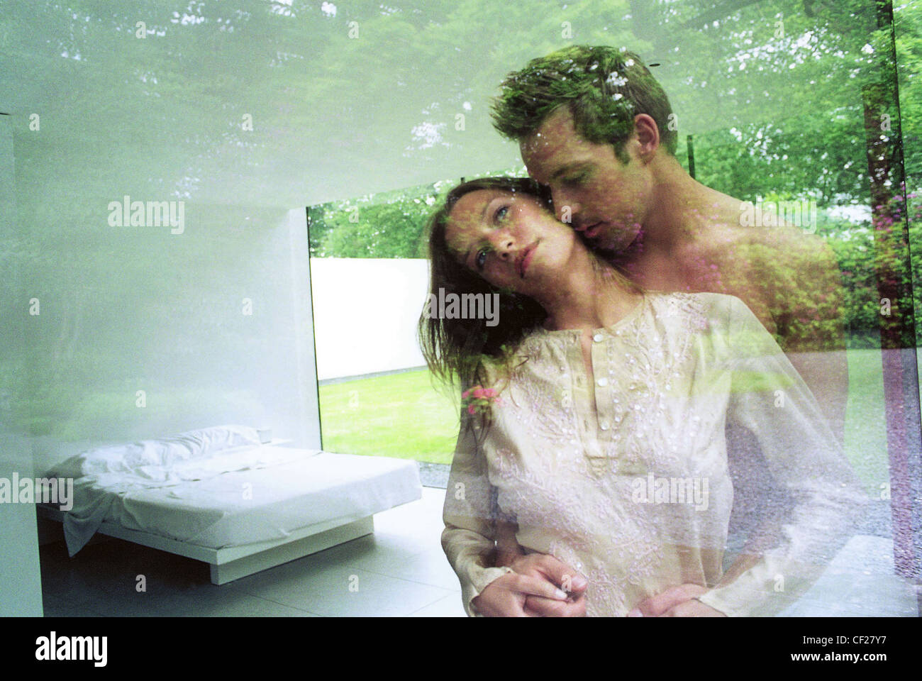 Couple cuddling in modern bedroom with floto ceiling glass windows ...