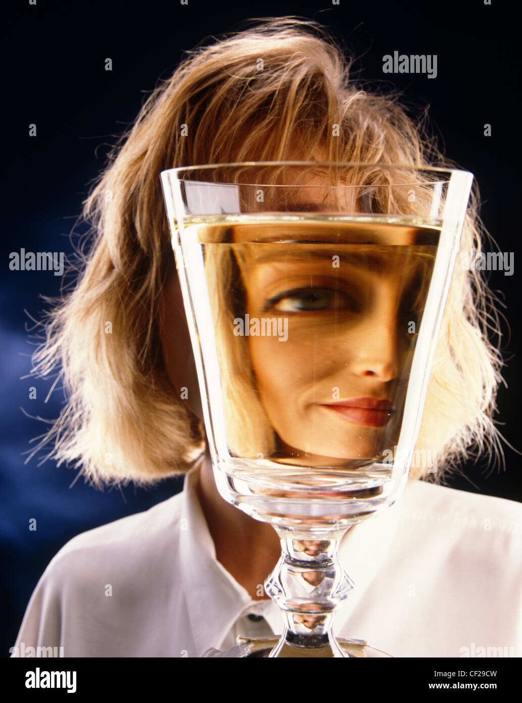 Female model with her face obscured and distorted by a glass of white ...