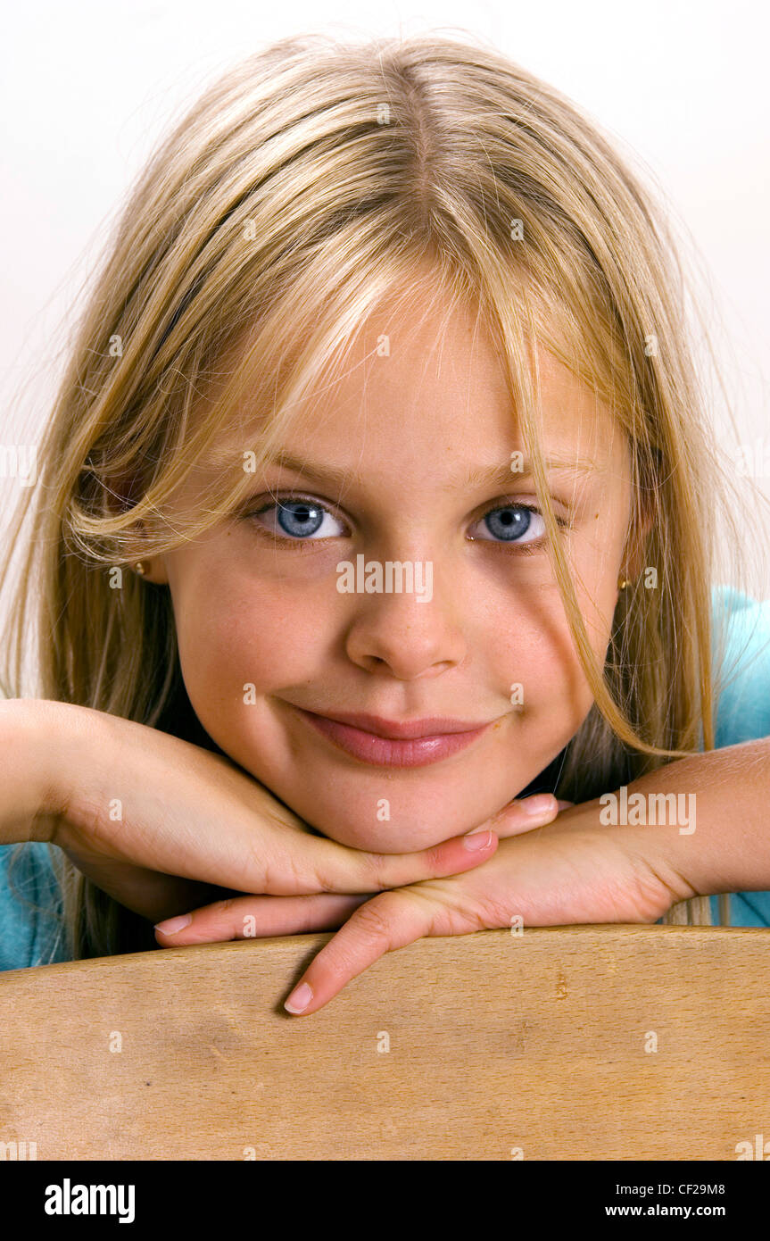 Female child leaning on the back of a chair with her hands under her ...