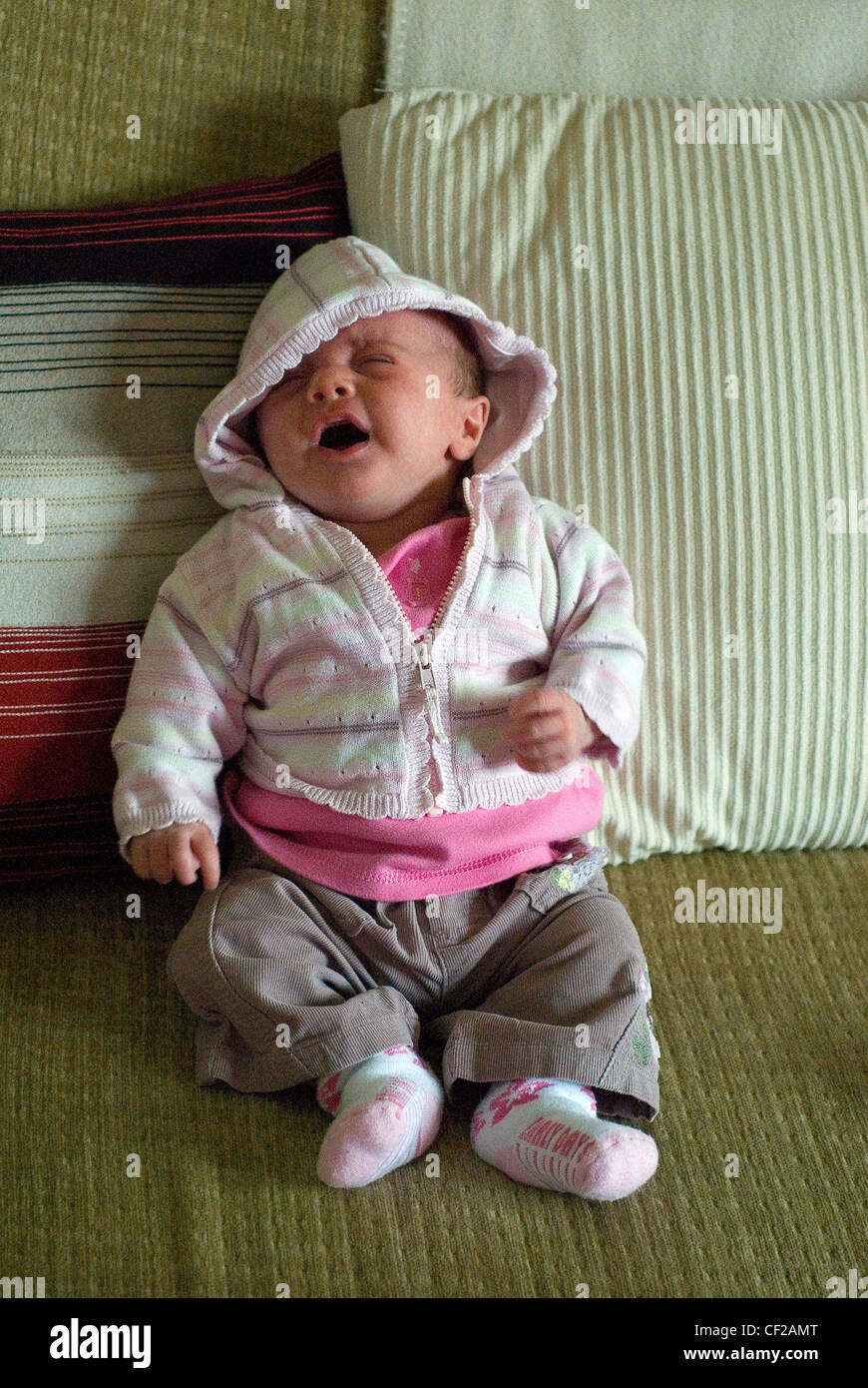 Female two month old baby propped up on a beige sofa, crying, dressed ...