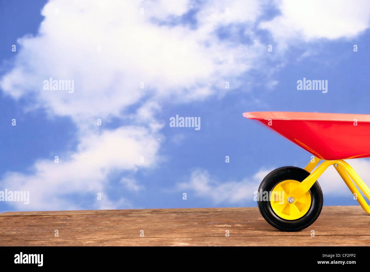 red and yellow wheelbarrow agains a blue sky with clouds Stock Photo ...