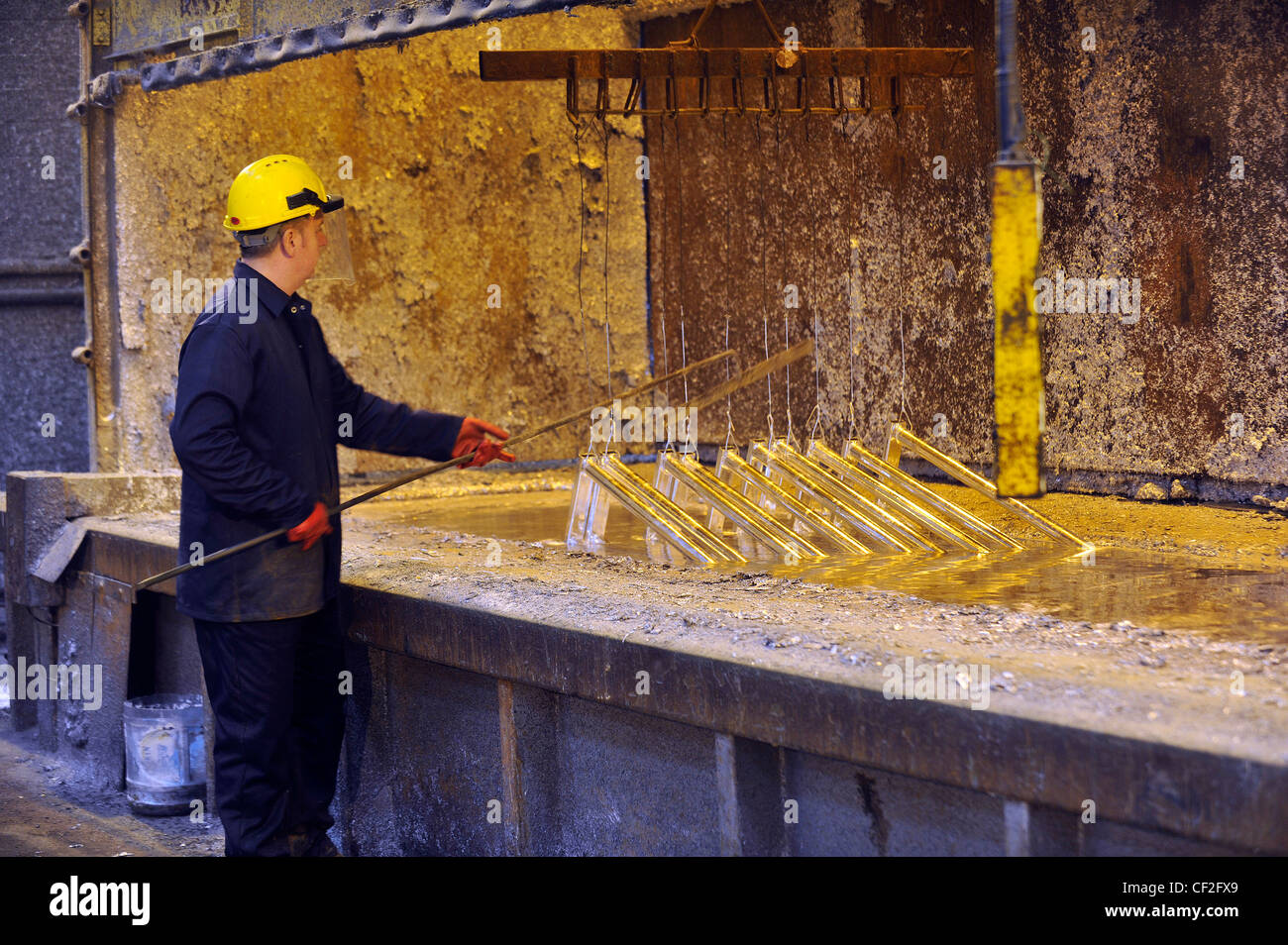 A worker prepares steel and skims molten zinc at a galvanizing plant ...