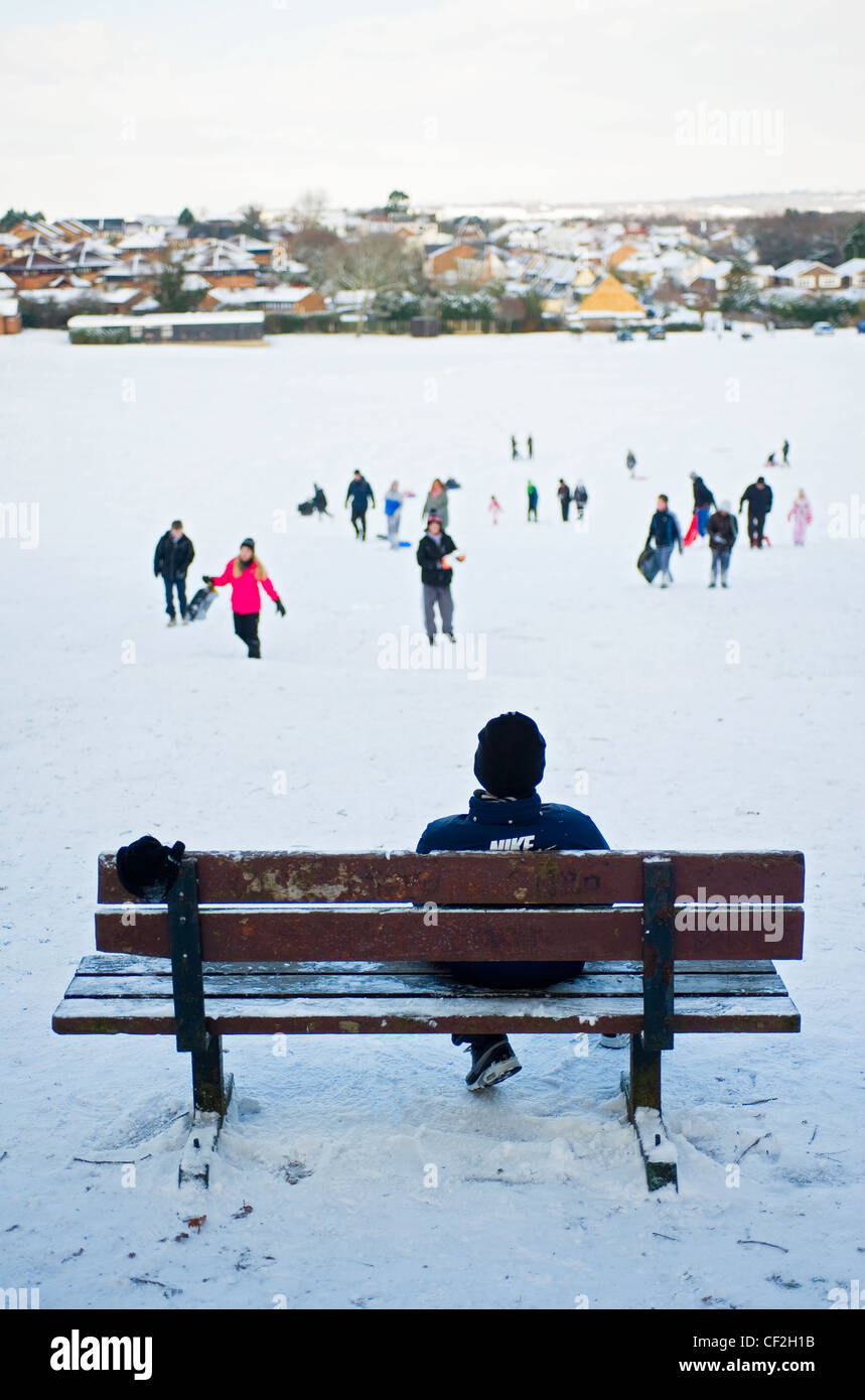 A young boy sitting on a bench watching children playing in the snow ...