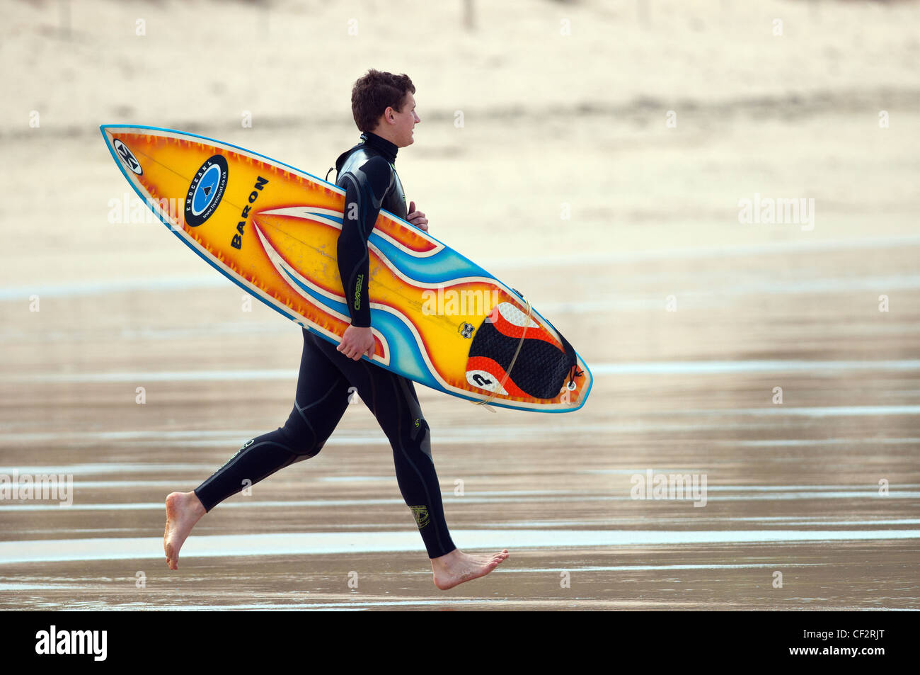 A surfer running across Fistral beach carrying his surfboard Stock ...