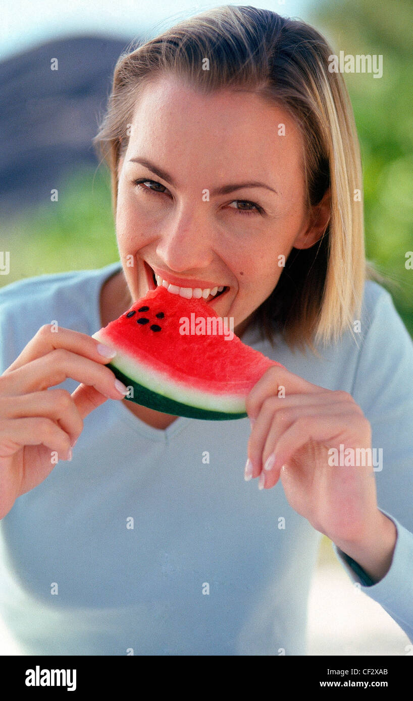 Female with shoulder length blonde hair wearing blue top, biting in to ...