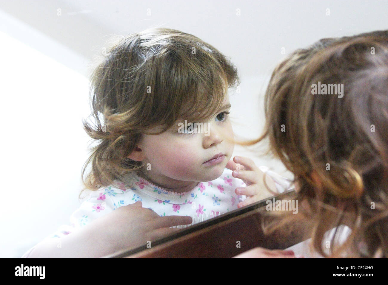 Female child with brunette hair looking at herself in mirrtouching face ...