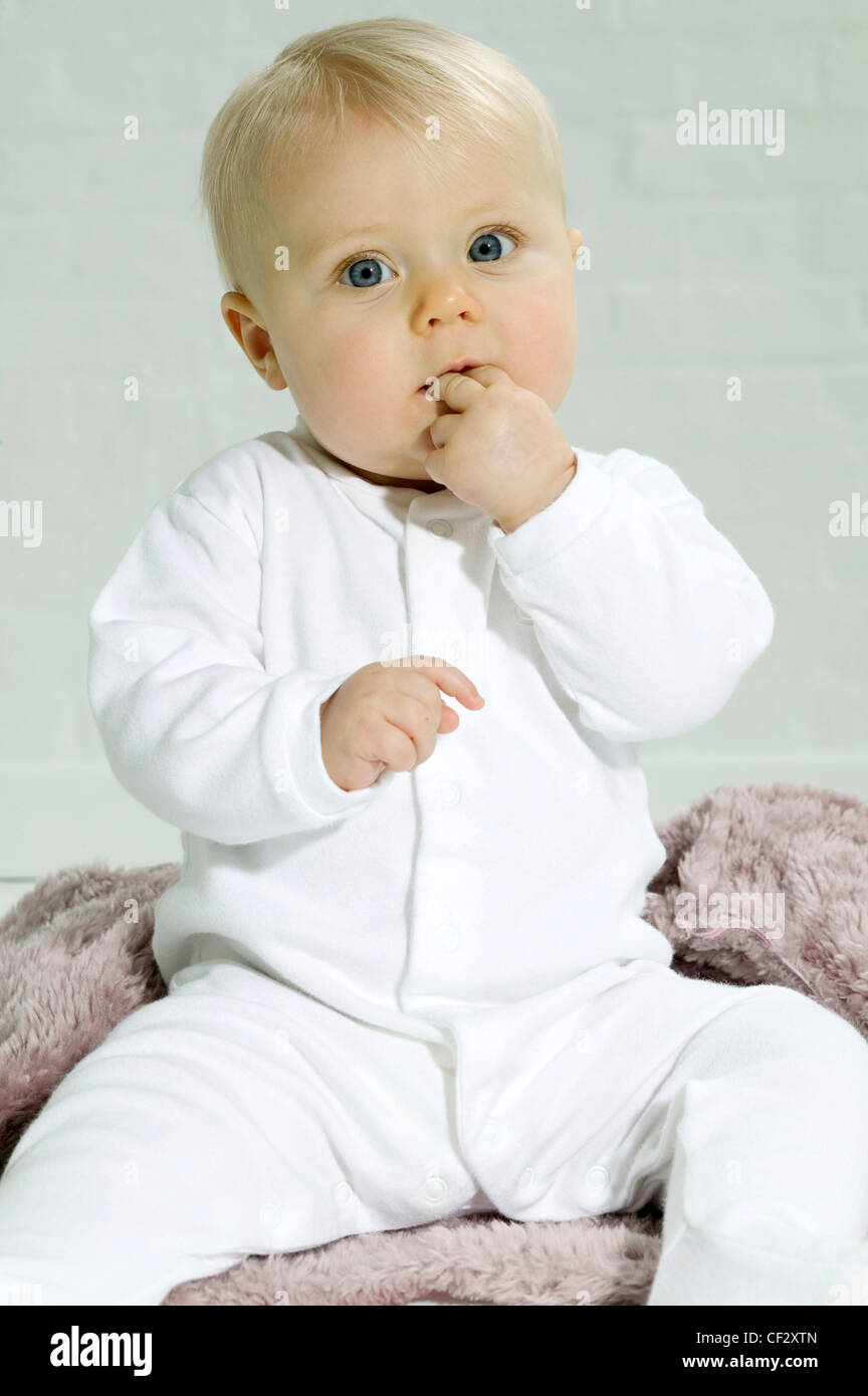 Female baby wearing white babygro sitting on grey fur blanket looking ...