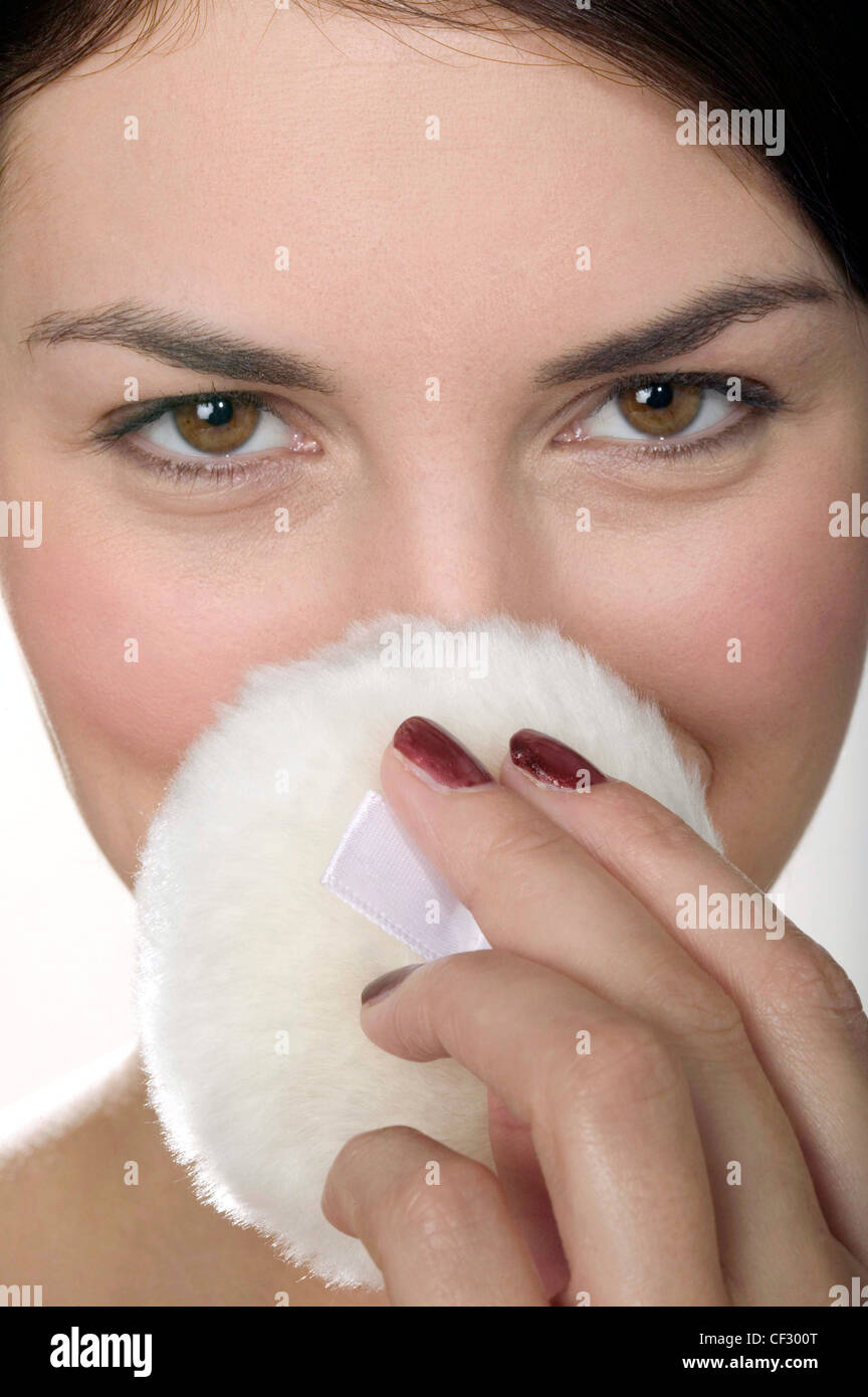 Female with brunette hair off face holding powder puff to nose ...