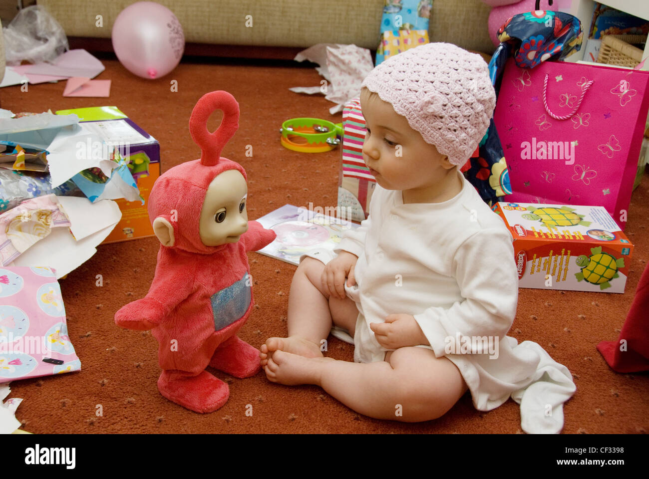 A female baby, wearing a white babygro and pink crocheted hat, sitting ...