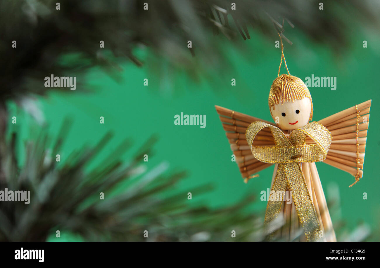 A straw angel shaped tree decorations hanging off the branch of a ...