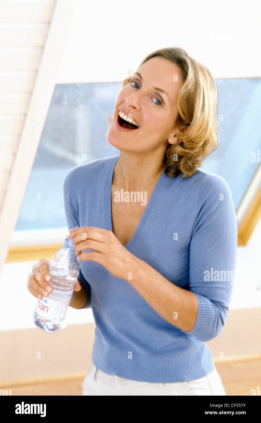 Female with short fair hair, wearing a blue top, holding a bottle of ...