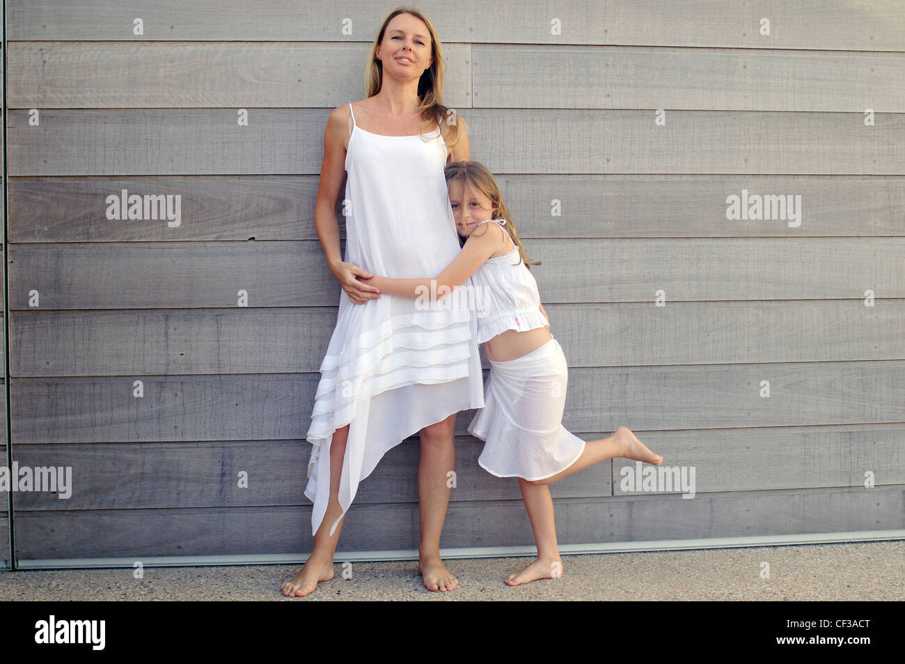 Mother and daughter wearing white dresses standing in front of a wall ...