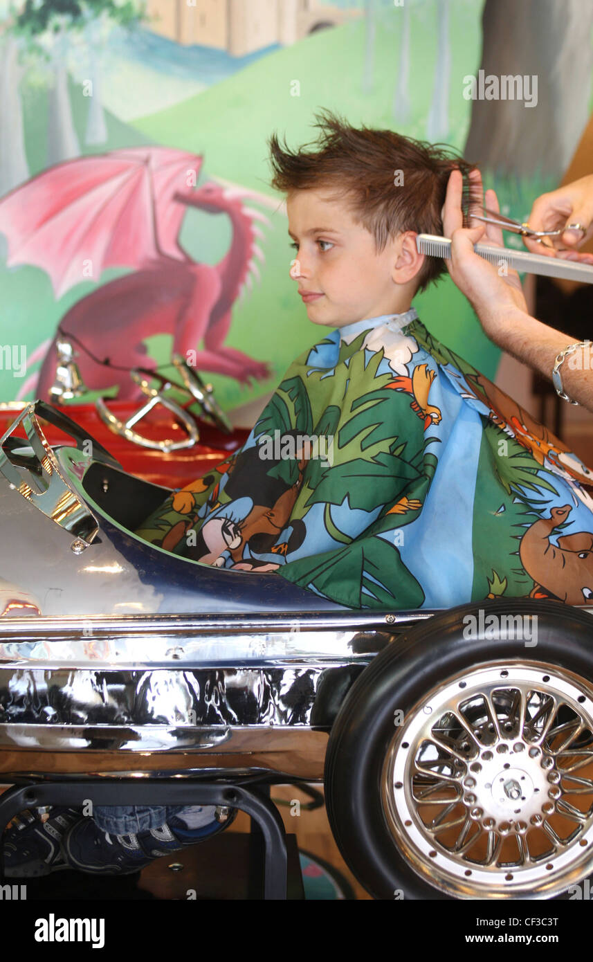 Eight year old male child sitting in a shiny toy car having his hair ...