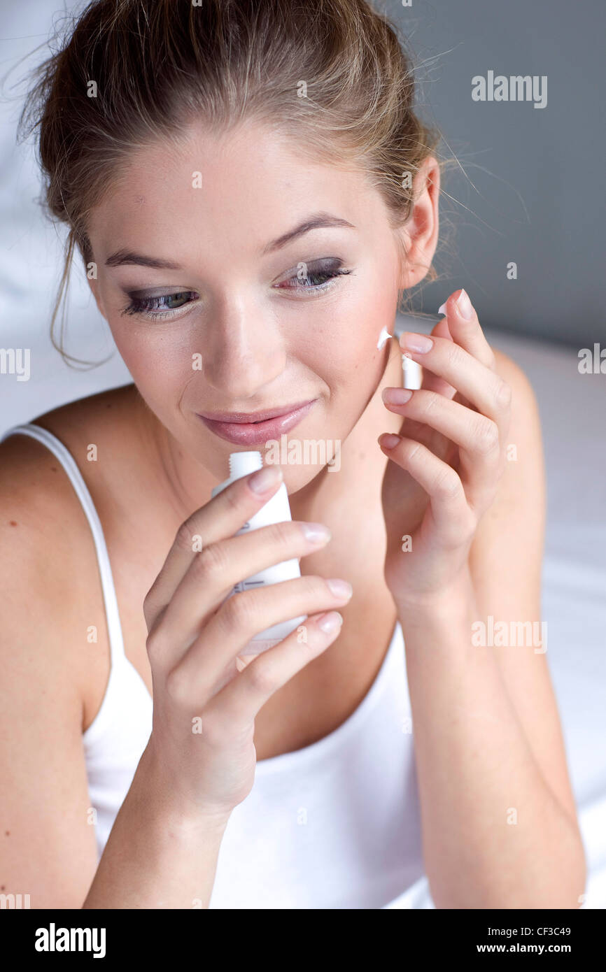 Female with brunette hair, wearing white camisole, applying face cream ...