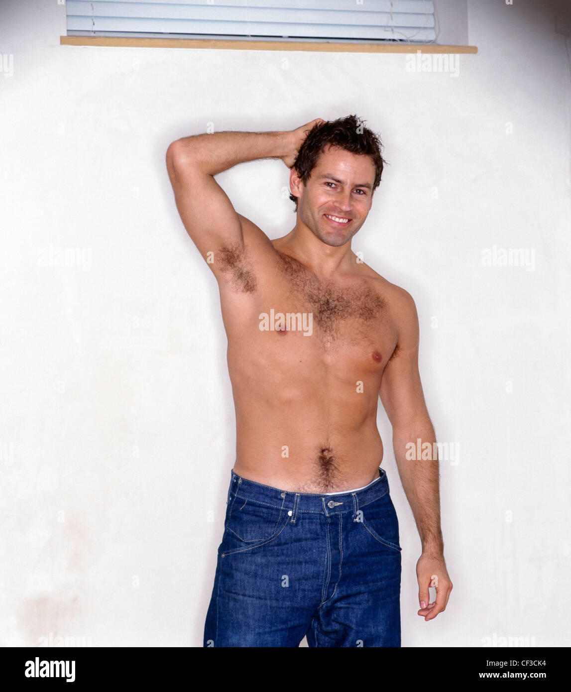 Male with brunette hair, wearing blue jeans, standing with one arm on ...