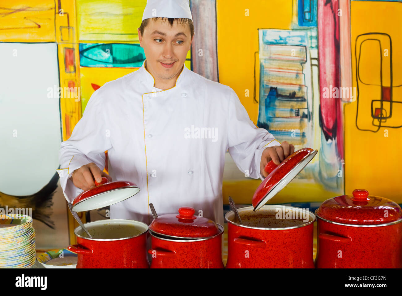 cheerful cook in uniform near red pans in public catering restaurant ...