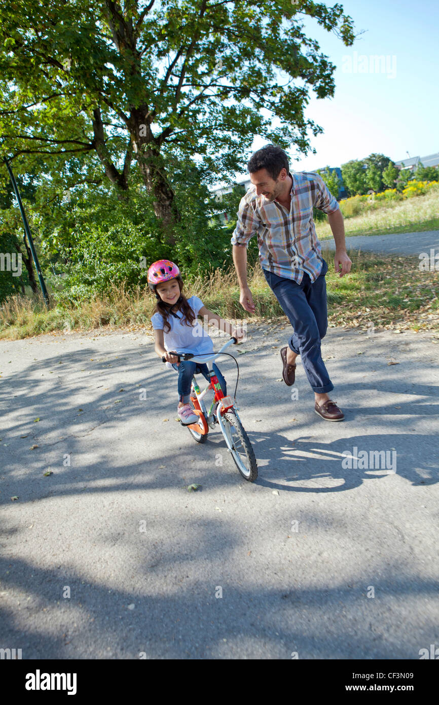 Father running next to daughter on bike Stock Photo - Alamy