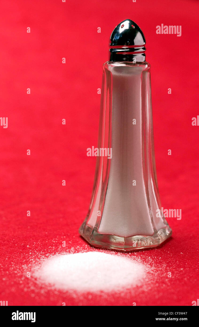 PIle of table salt on red surface by glass and chrome salt shaker Stock ...