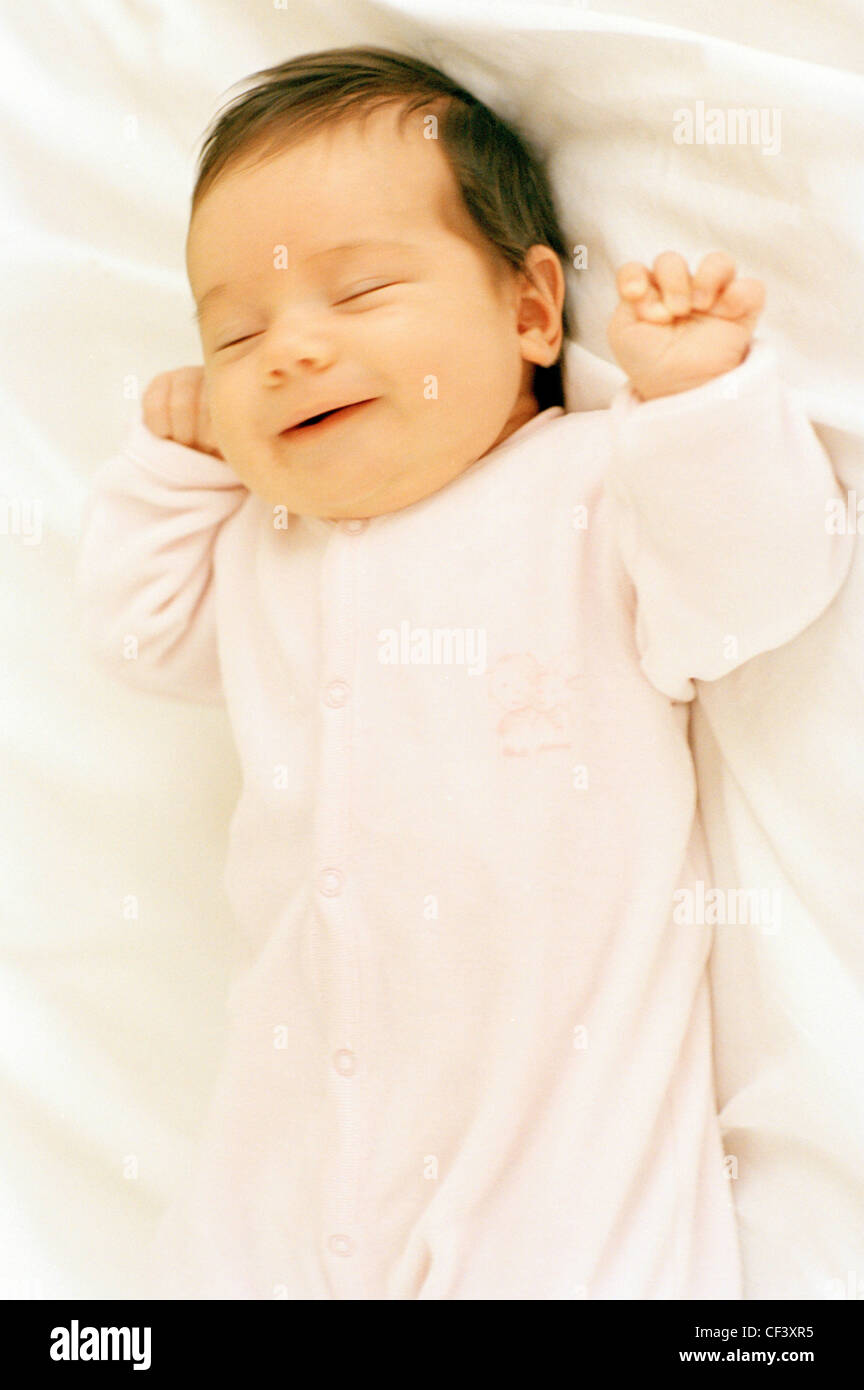 Baby with dark brown hair in pink babygro lying on back on covers eyes ...