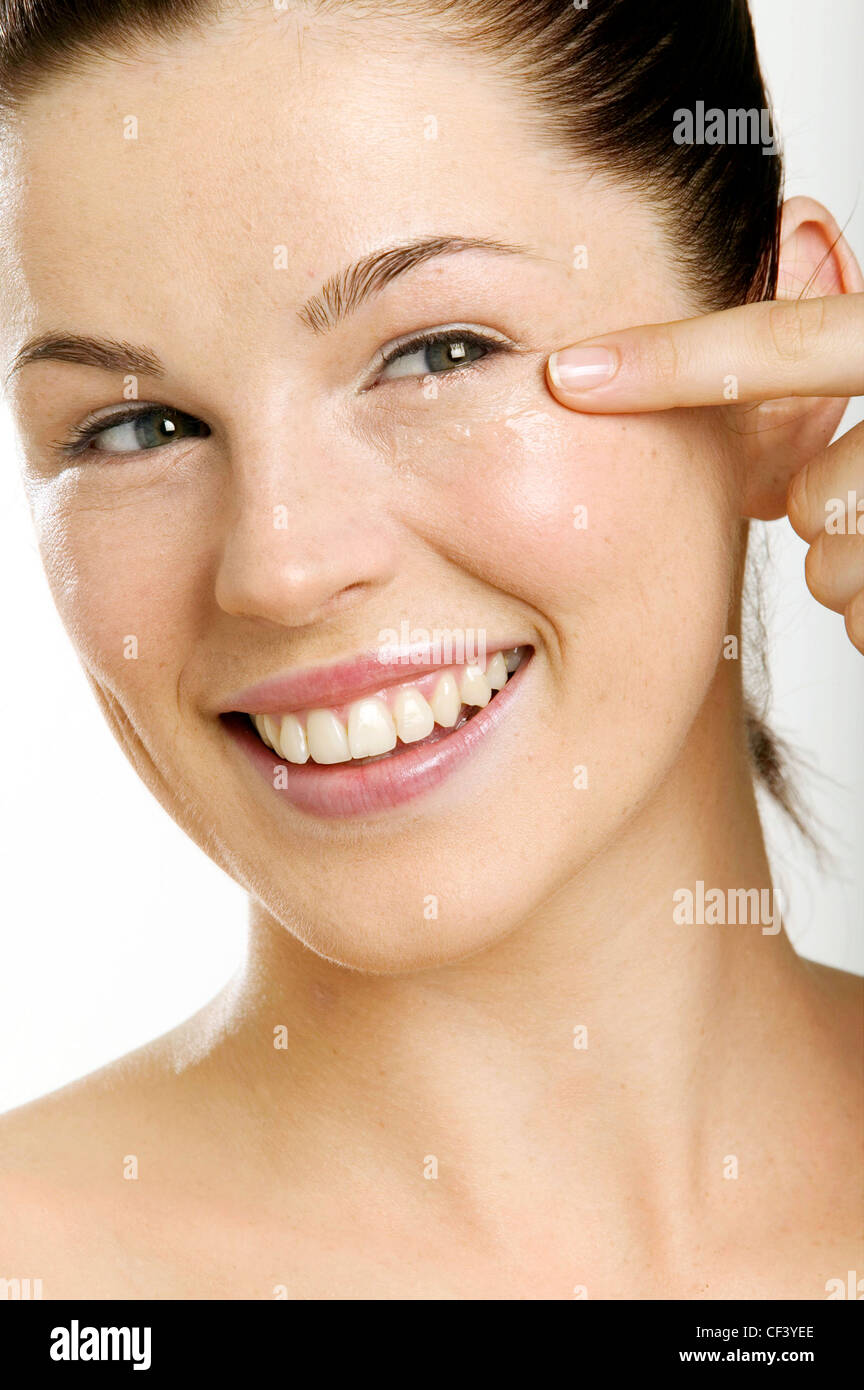 Female rubbing in clear eye gel under eye with finger, looking to ...