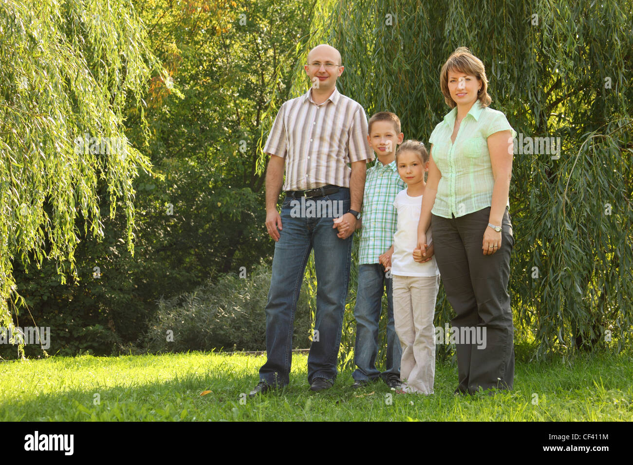family with two children is standing near osier in early fall park ...