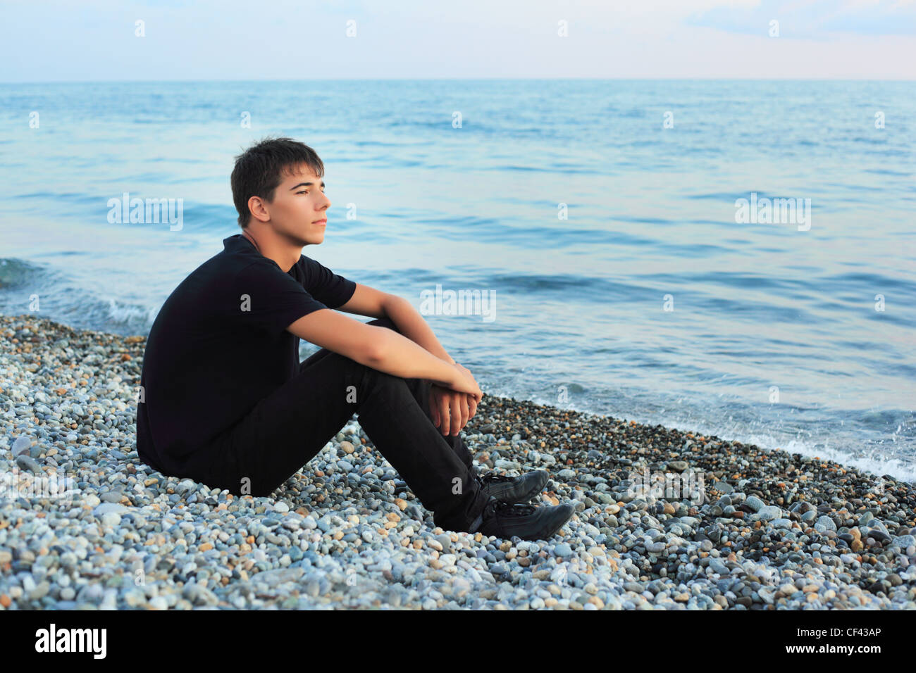 sitting teenager boy on stone seacoast, Looking afar Stock Photo - Alamy