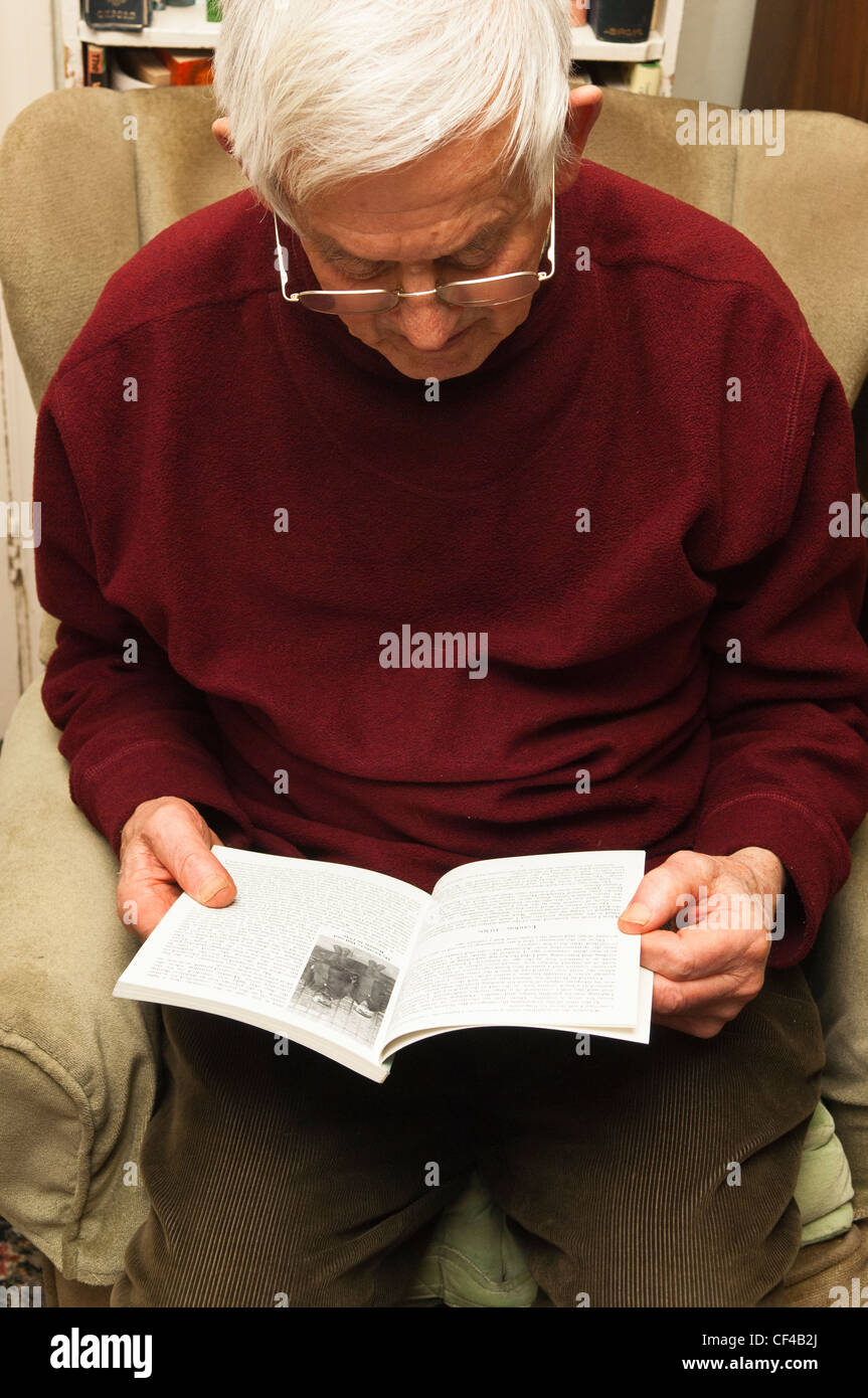 A senior elderly man in his 80's reading a book at home in England ...