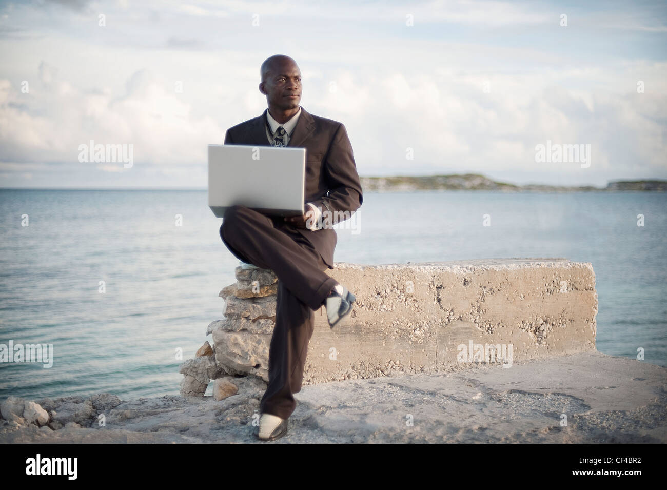 A Businessman With A Laptop Computer Sitting On A Rock Ledge At The ...