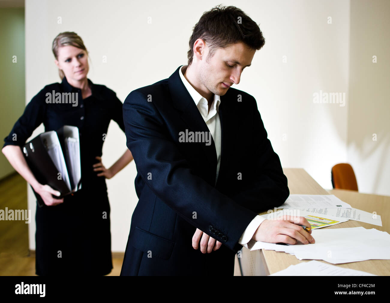 Office life scene. Young businessman signing documents and young ...
