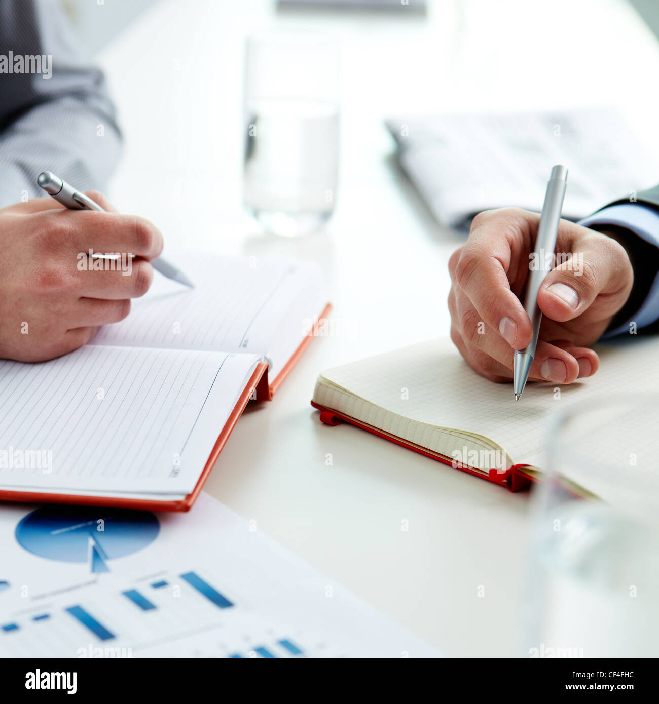 Close-up of male and female hands with pens over open notebooks at ...