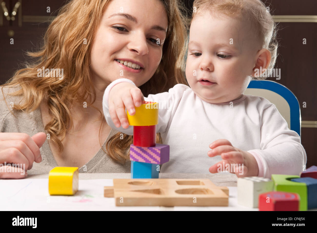 Young mother and her little baby daughter building tower with toy ...