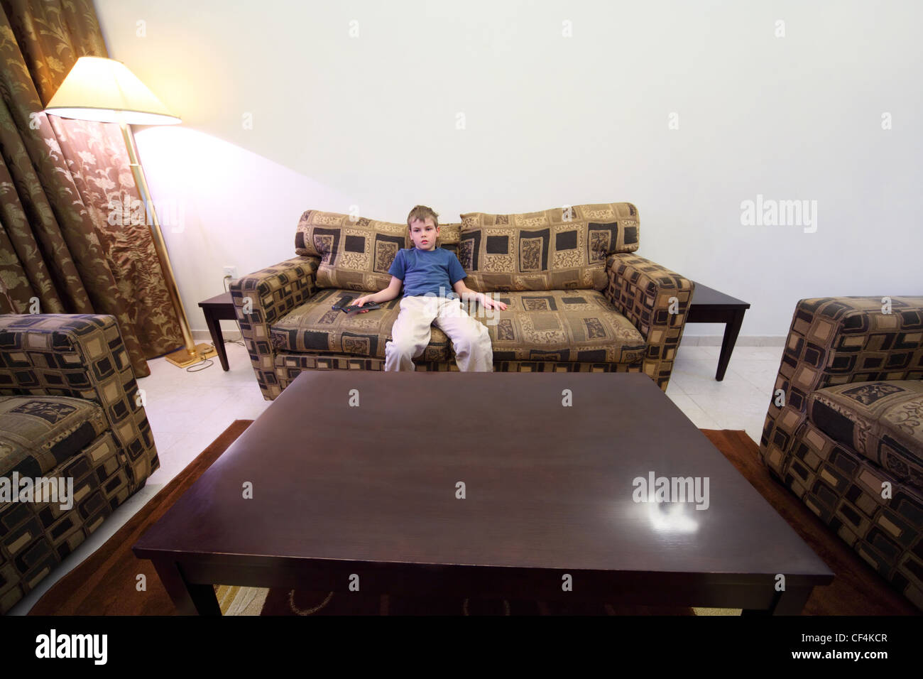 little boy with remote control sitting at brown sofa in room with white ...