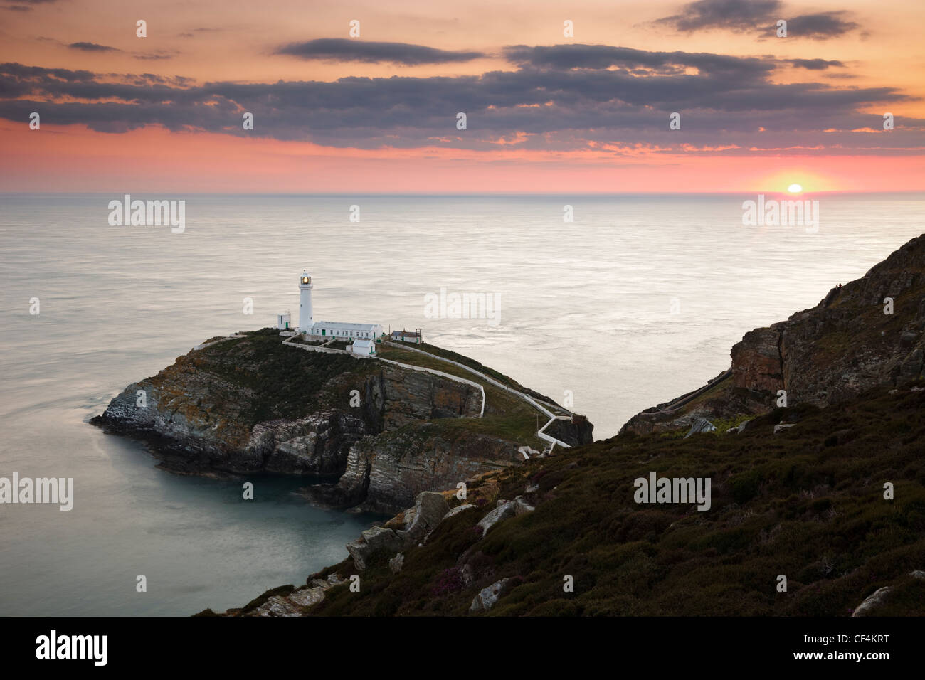 The sun setting on the horizon behind South Stack Lighthouse, a ...