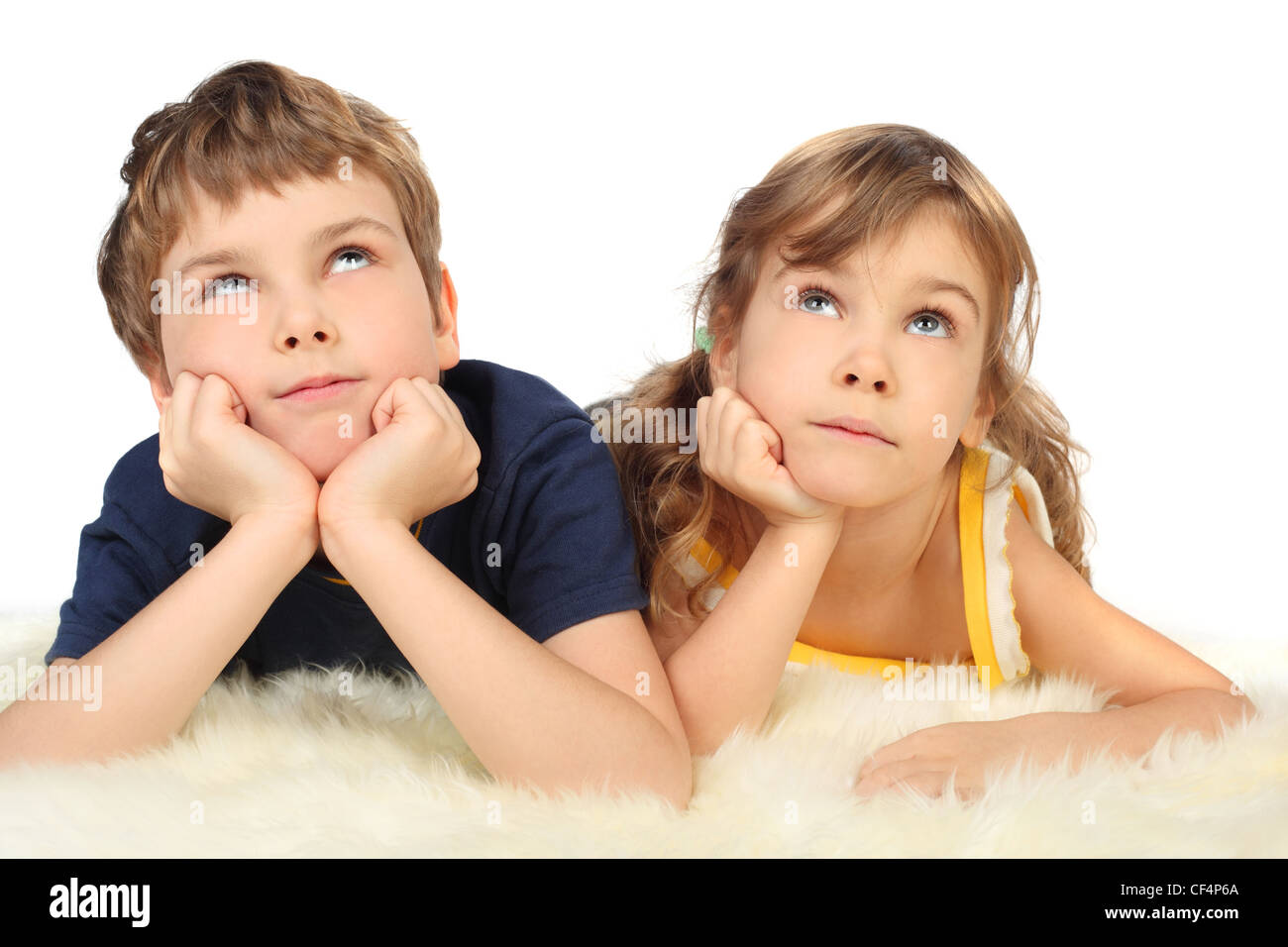 little boy and girl lying on white fell, chin on hands, looking up ...