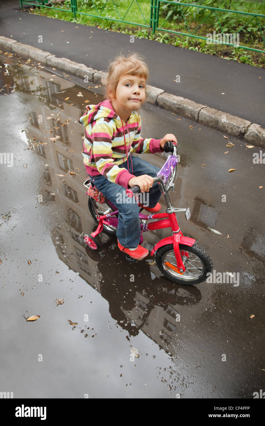 little girl goes on a bicycle on wet asphalt, reflexion in puddle Stock ...