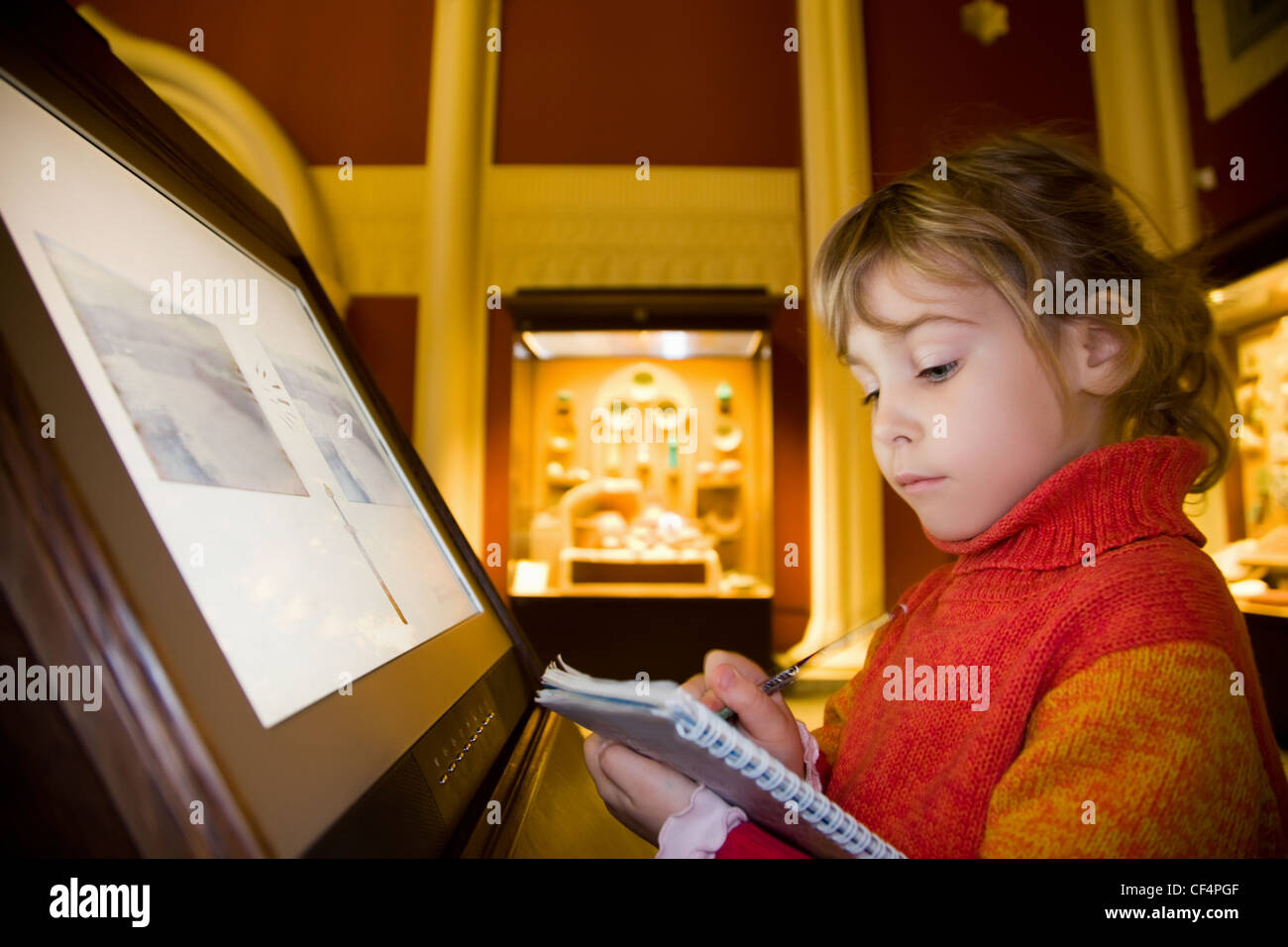 little girl standing near monitor writes to writing-books at excursion ...