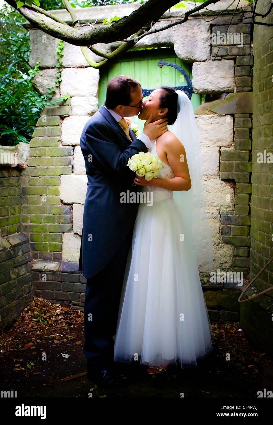 Wedding couple are kissing under tree. A groom is holding bride's neck ...