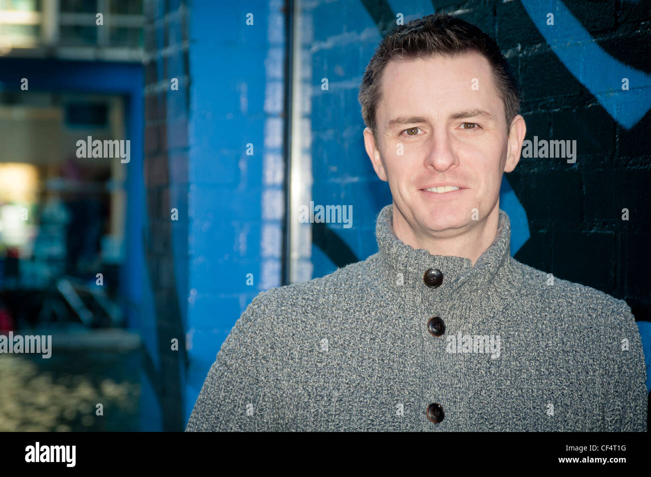 Portrait of young man leaning against a wall while standing outside. hi ...