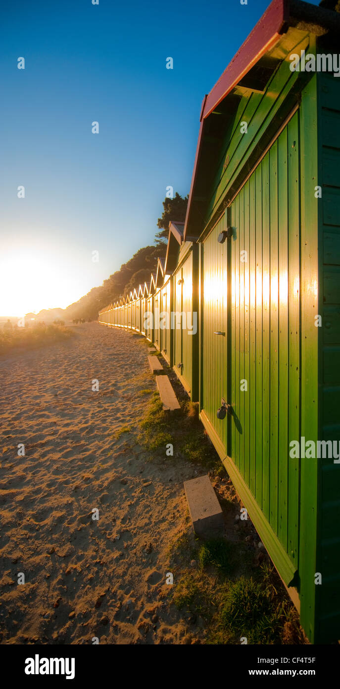 Sunrise over beach huts stretched out along Avon Beach in Christchurch ...